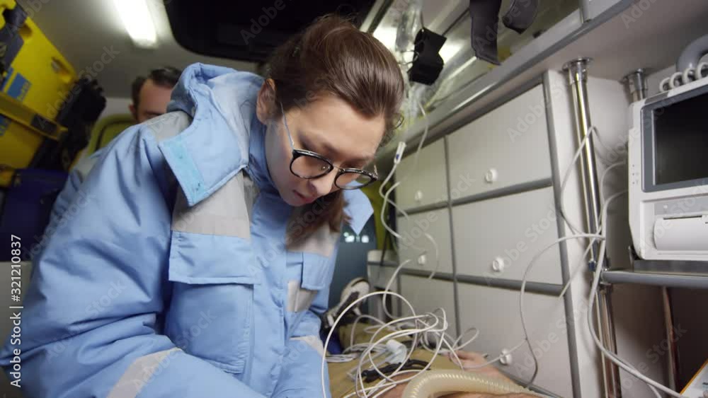 Handheld tracking of serious female paramedic putting IV needle into ...