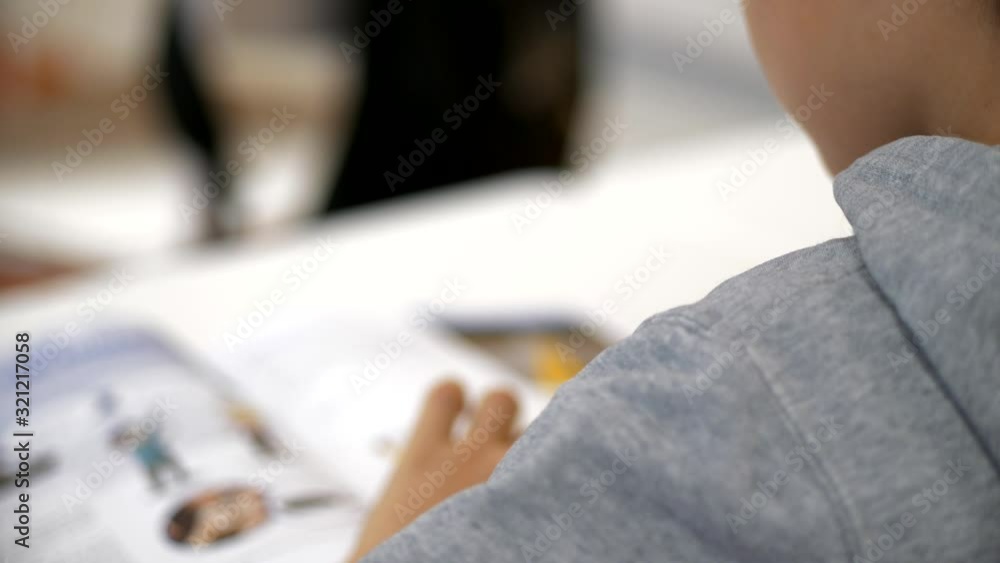 Rear view of Caucasian school boy reading a book in classroom ...