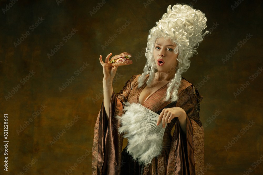 Eating burger delighted. Portrait of medieval young woman in brown ...