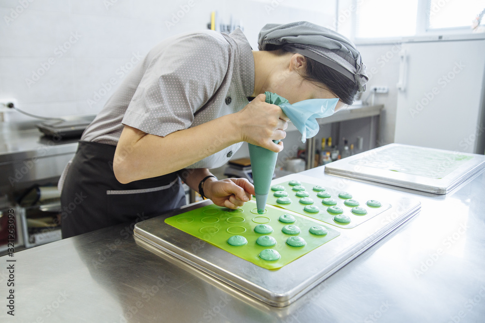 Making pink macarons. Piping out pink macaron mixture on a slip mat on ...
