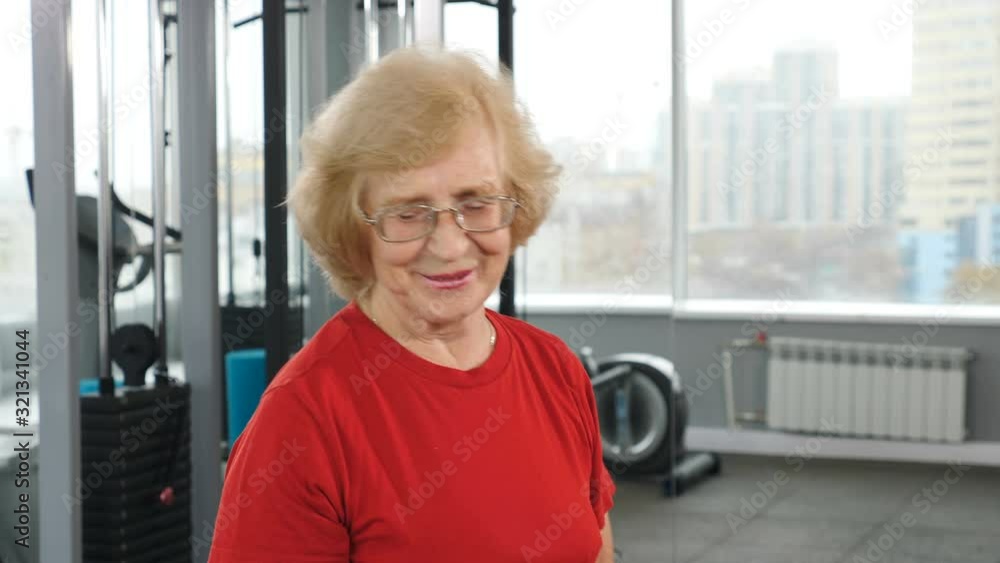 Portrait of old pleasant woman lifting barbells for pectoral training ...