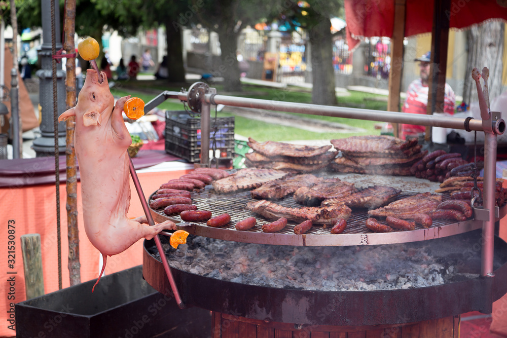 Piglet, ribs and grilled pork sausages on a giant circular grill at a ...