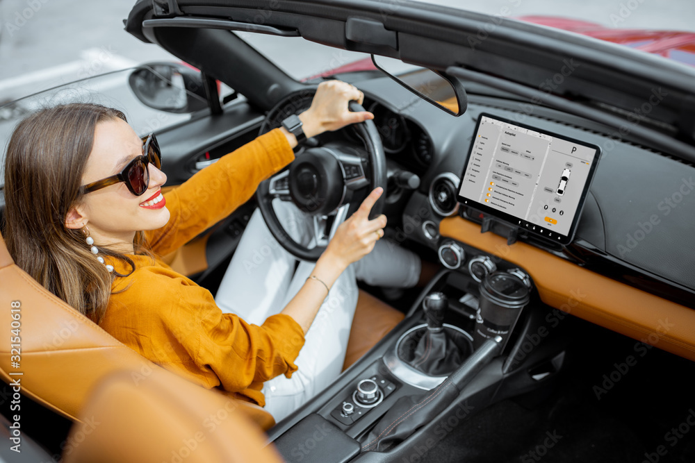 Young and cheerful woman driving sports car with a digital touchscreen ...