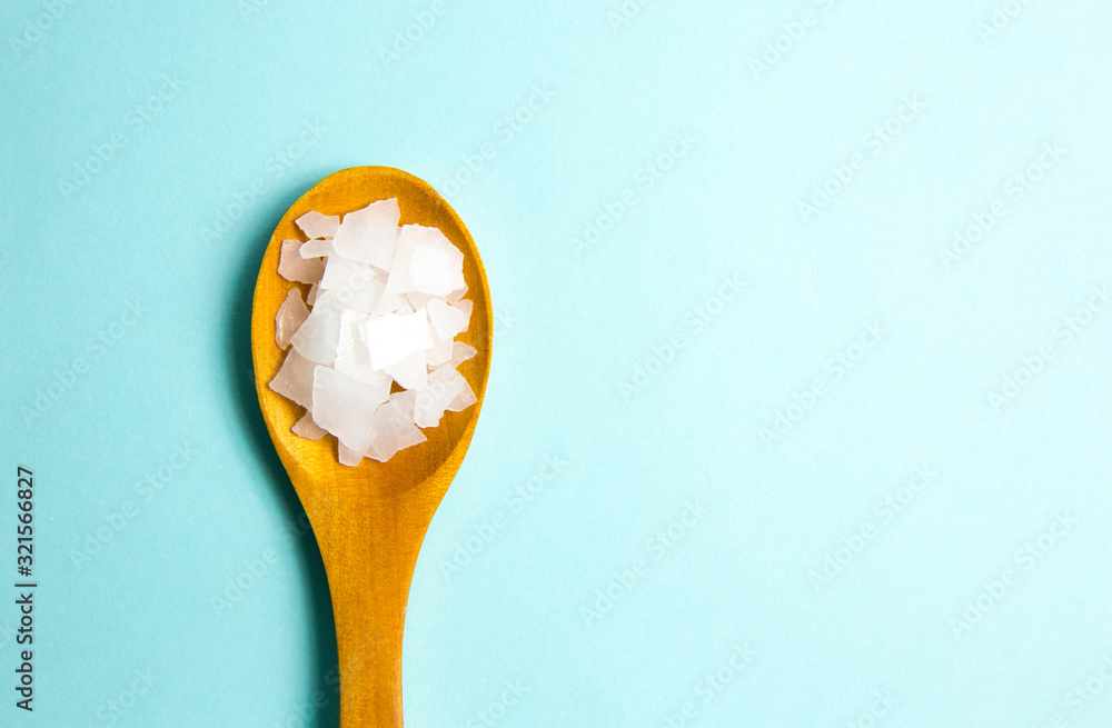 Magnesium Chloride Flakes scattered around brown wooden spoon on blue ...