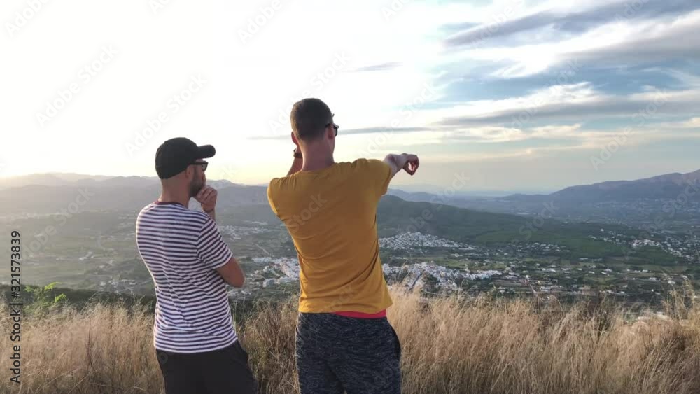 Back view of two young men standing at the top of the hill. Tourist ...