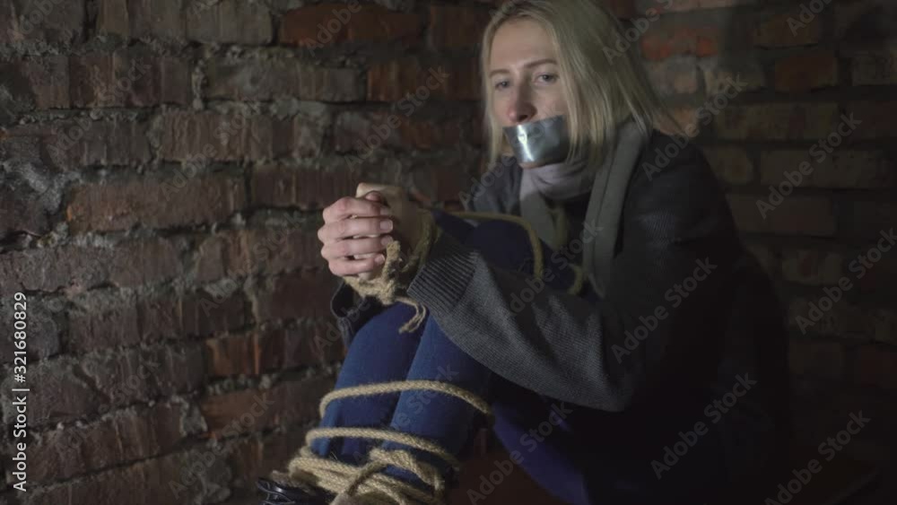 woman trying to free her hands from the rope. Sits in the basement ...