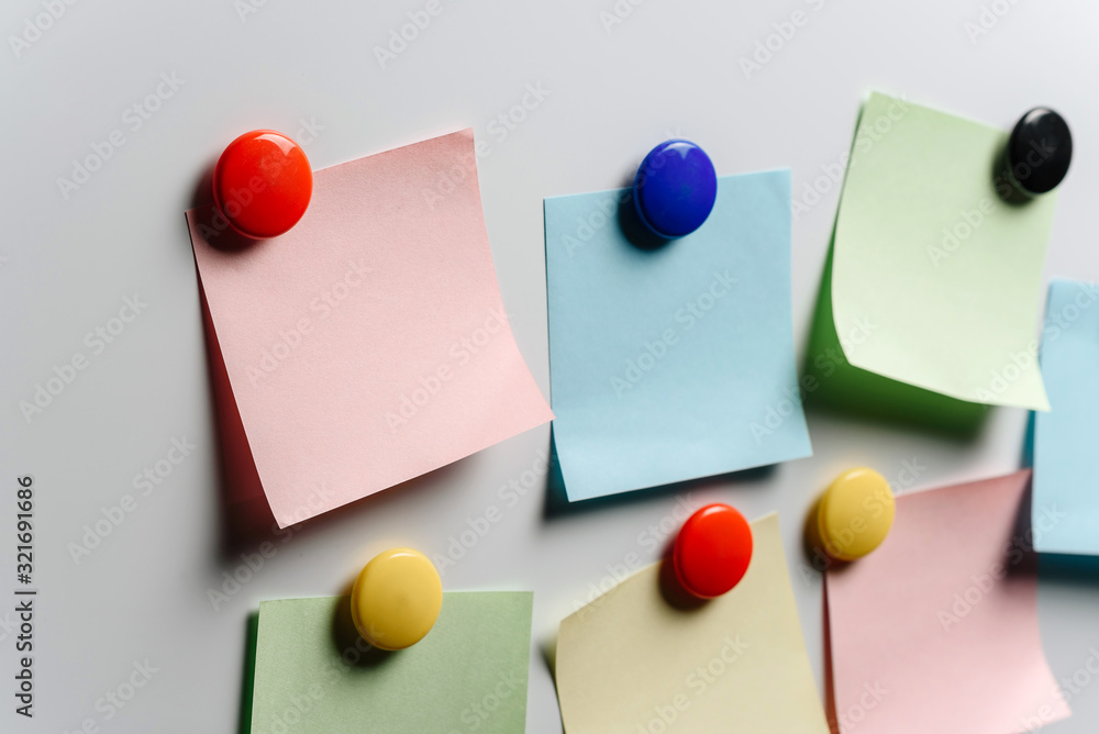 Colored notes for writing are attached with magnets to a white surface ...