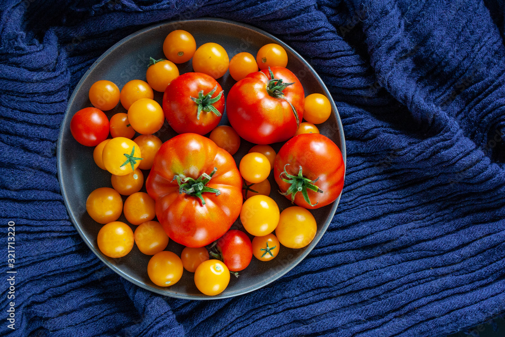 Fresh colorful tomatoes in a plate on a dark blue background ...
