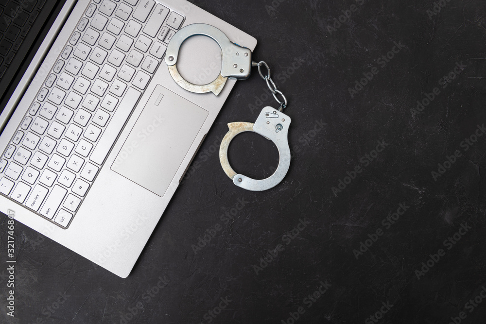 Handcuffs and laptop on dark background top view. Piracy, internet ...