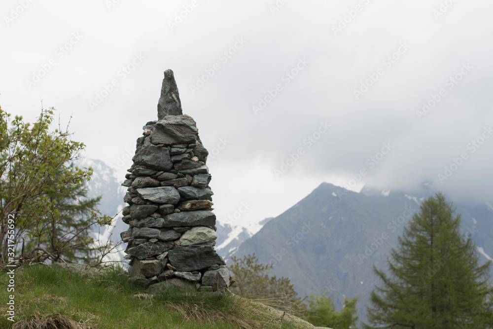 Stone pile grave in a grass field, background is a moody mountain ...