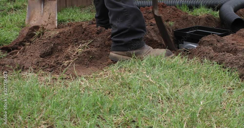 Worker digging out a trench to fit a new french drain pipe system in ...