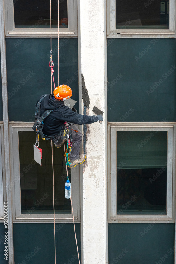 Foto de trabajador vertical colgado de una cuerda reparando una fachada ...