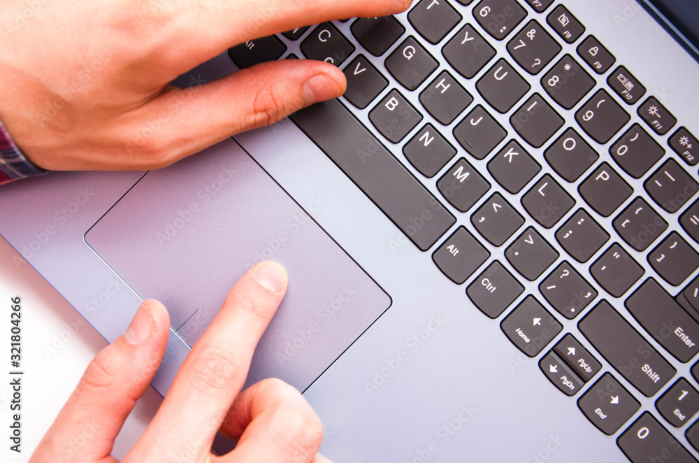 Men's hands in a shirt in a cage lie on the keyboard on a laptop from a ...