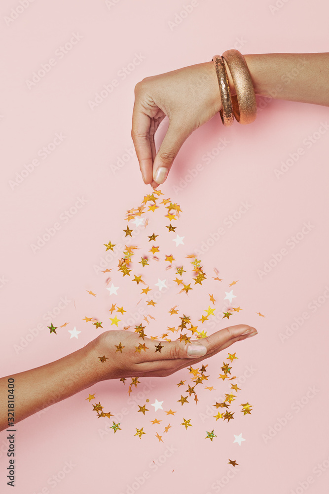 Female hand sprinkles gold confetti stars decoration on hand on pastel ...