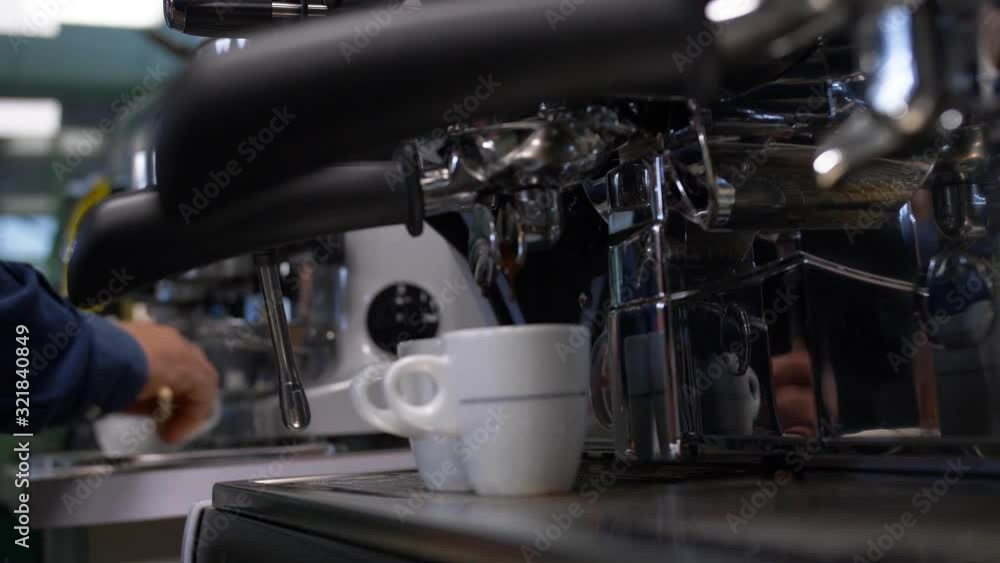 Two white cups into which black coffee is poured from a large metal ...