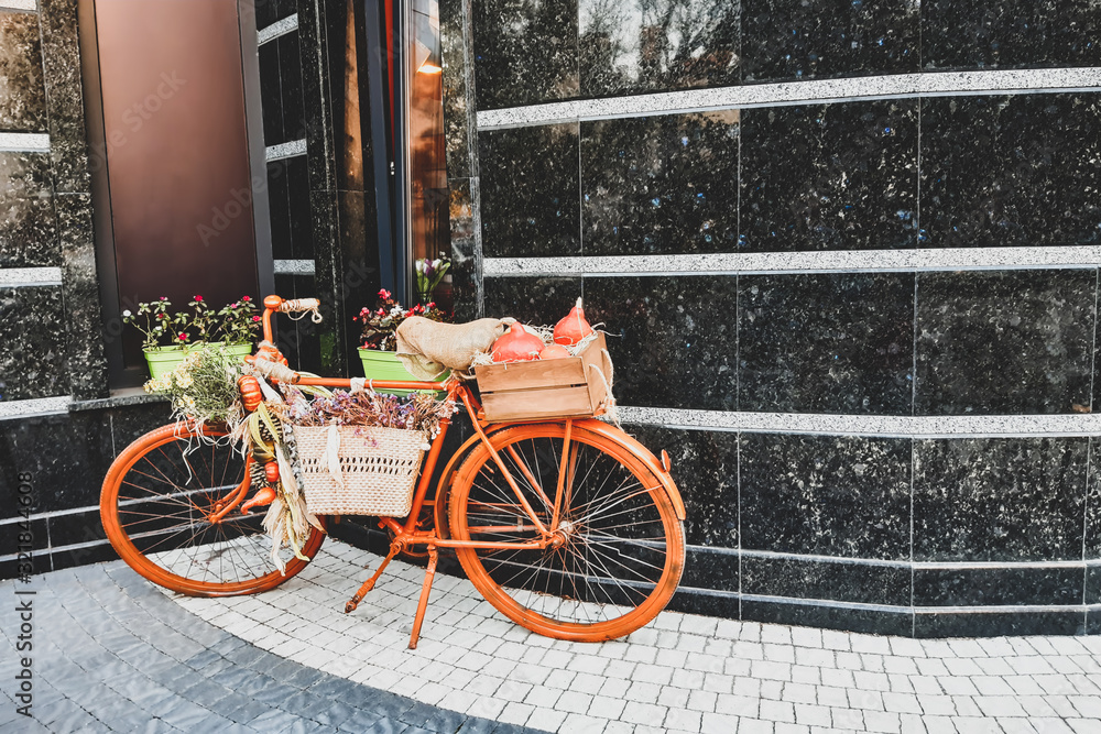 Decorative painted in orange color bicycle in the alley with a basket ...