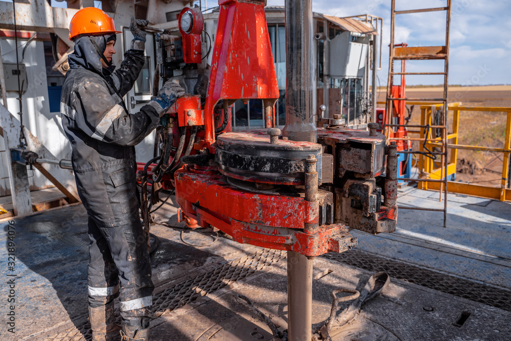Work driller in red uniform, in helmet and goggles. He uses a hydraulic ...