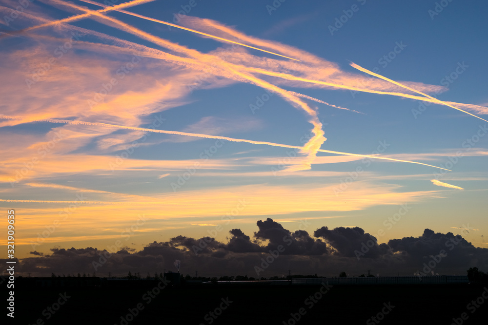 Colorful contrails high up in the sky are illuminated by the light of ...