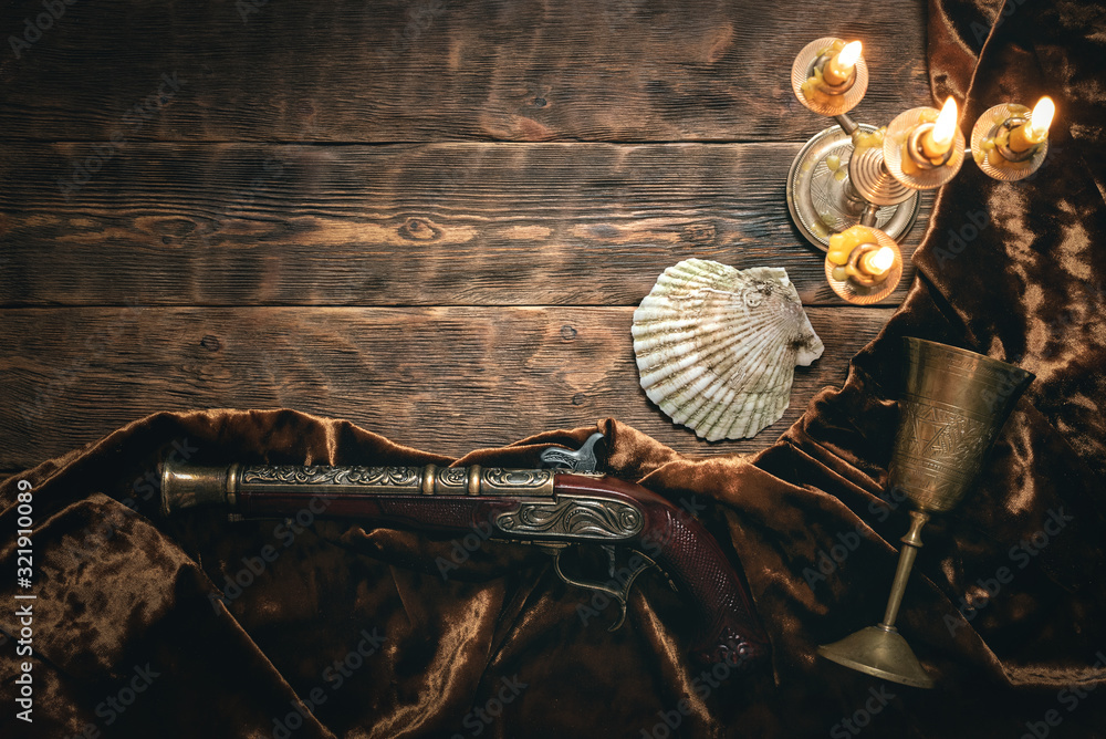 Old musket gun, seashell and golden goblet on pirate desk table in the ...