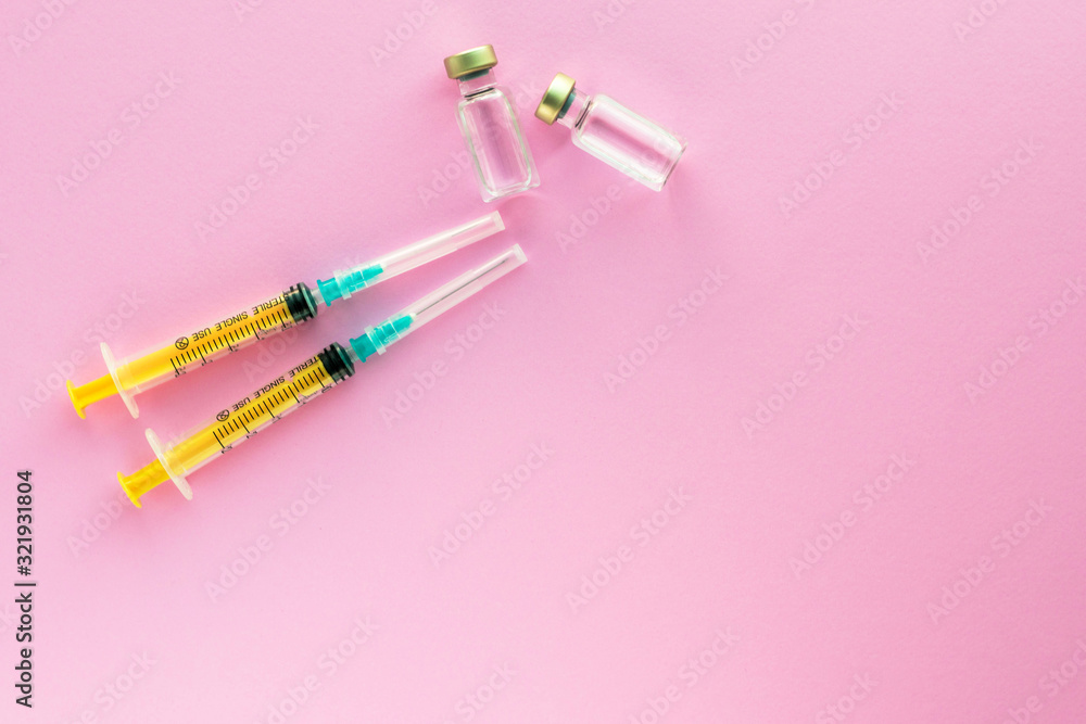 Two syringes and glass vials with liquid on light pink background ...
