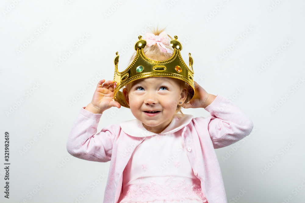 Little child girl in a dress tries on a crown on a light background ...