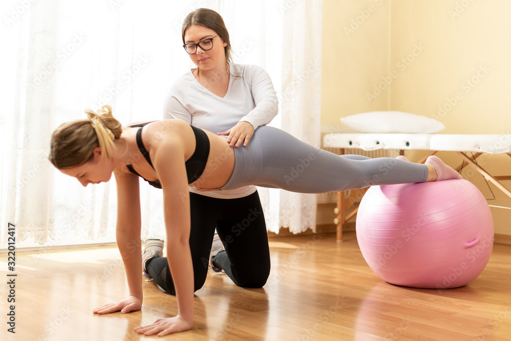 Physiotherapist working with young female client on core strength using fitball. Rehabilitation ...