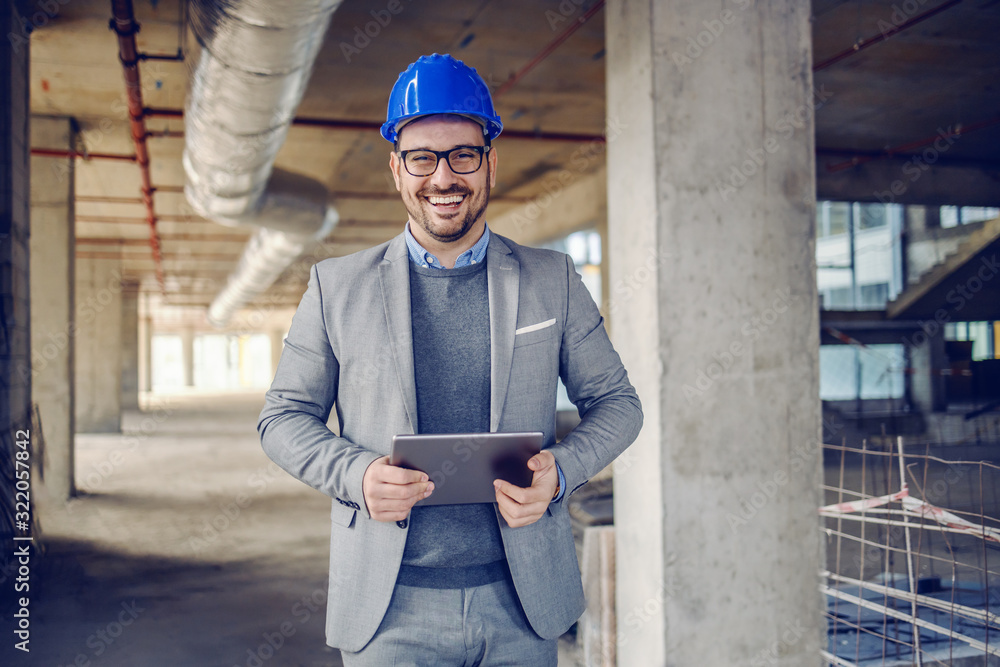 Handsome cheerful caucasian unshaven architect in suit, with helmet on ...