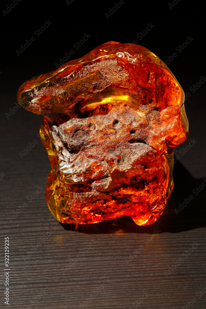 Bright translucent piece of amber with a natural crust on a black ...