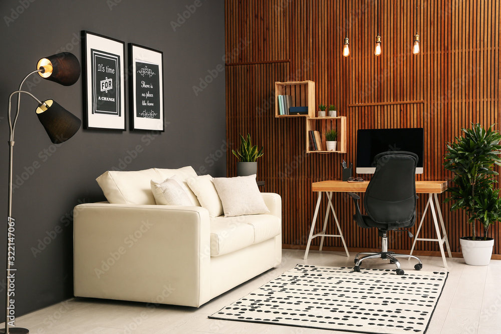 Comfortable workplace with computer near wooden wall in stylish room ...