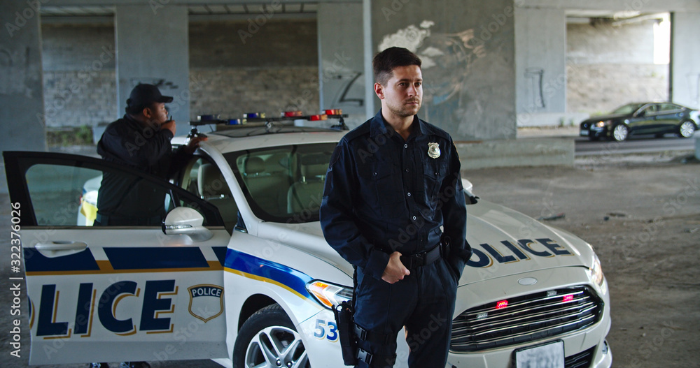 Confident cheerful policeman standing by car smiling of joy at work ...