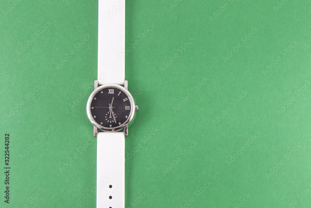 Wristwatch with a black dial and a white strap (bracelet) on a green ...