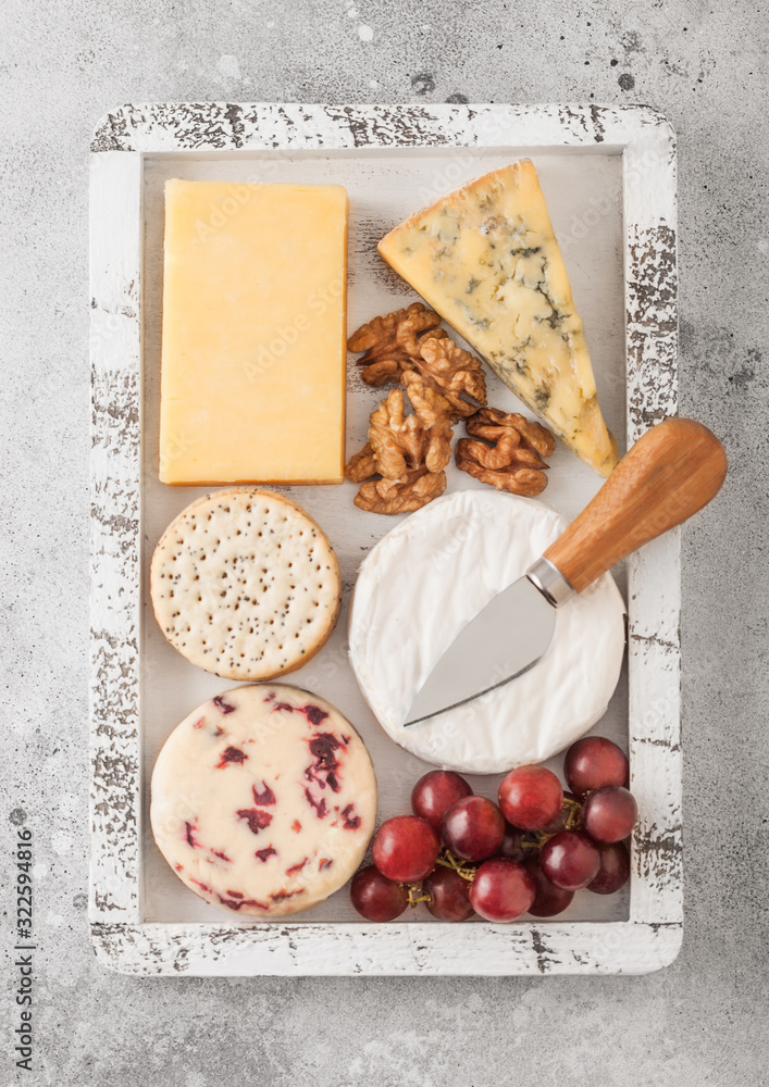 Selection of various cheese in wooden box with grapes and nuts on light ...