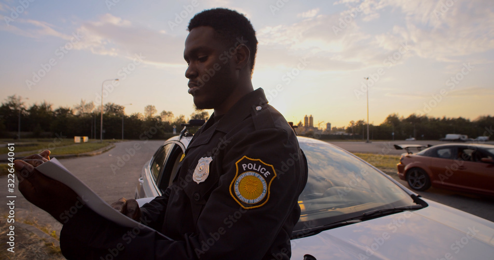 Handsome concentrated young policeman on duty writing down notes ...