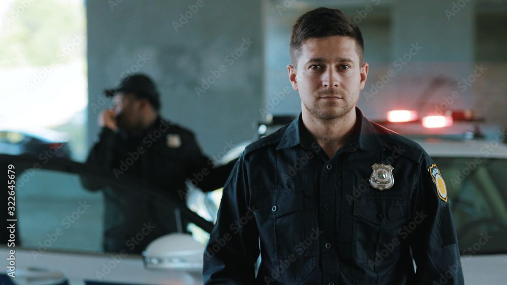 Portrait serious young man cops stand near patrol car look at camera ...