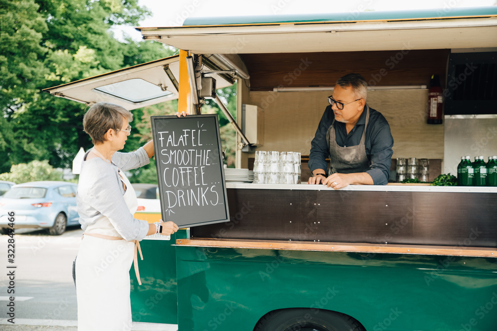 Female owner positioning board on concession stand while male coworker ...