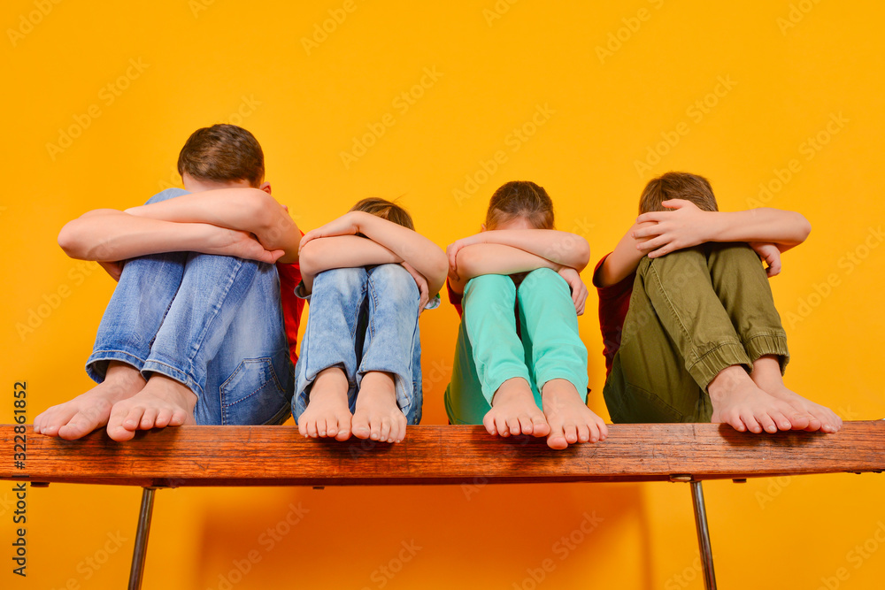 Barefoot children sit with their legs crossed and hugging their knees ...