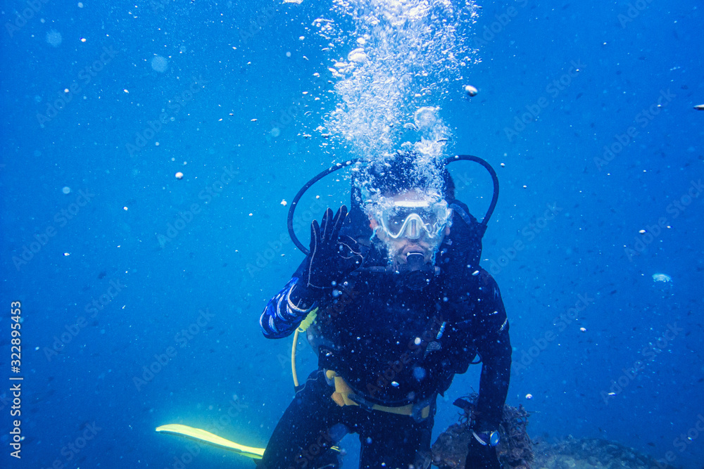 Scuba diver diving on tropical reef with blue background and reef fish ...