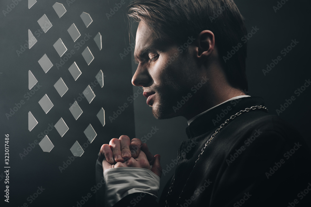Poster young thoughtful catholic priest praying with closed eyes in ...
