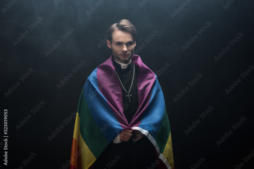 serious catholic priest wrapped in lgbt flag while looking at camera on ...