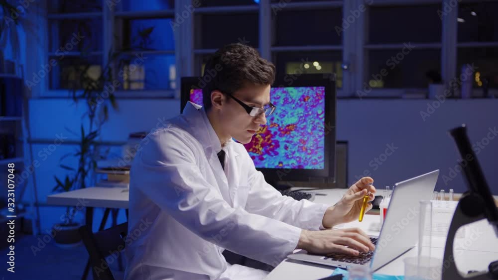 Tilt up of young scientist in lab coat and eyeglasses examining test ...
