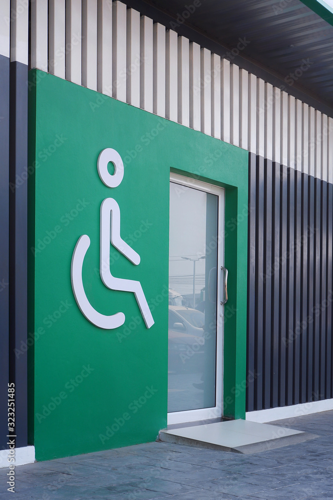 White disabled wheelchair sign with glass door on green wall and wooden ...