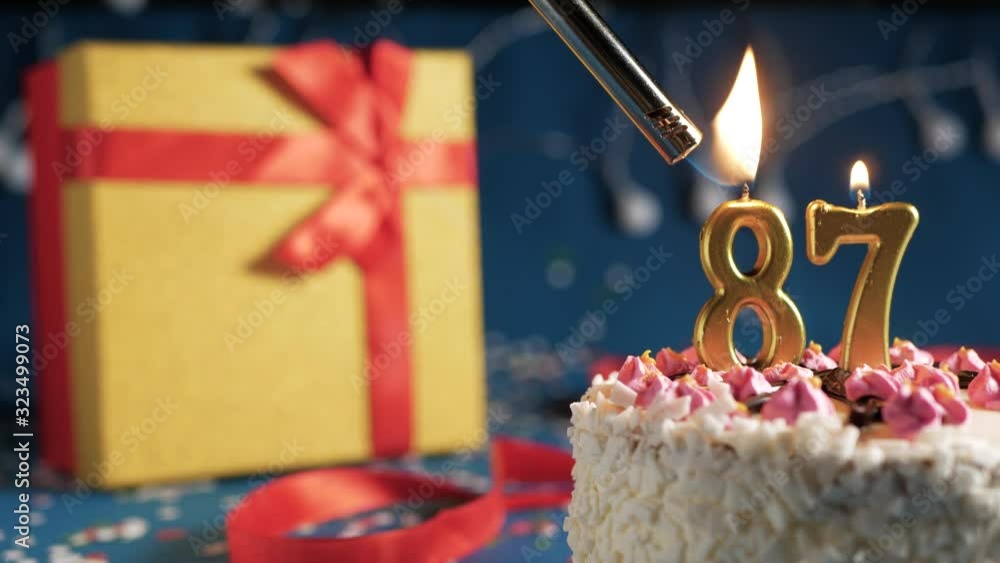 White birthday cake number 87 golden candles burning by lighter, blue ...