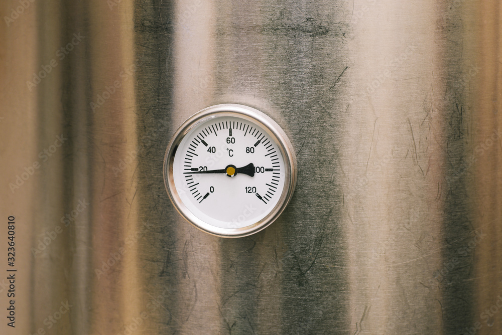 An industrial thermometer is mounted on a stainless steel boiler ...