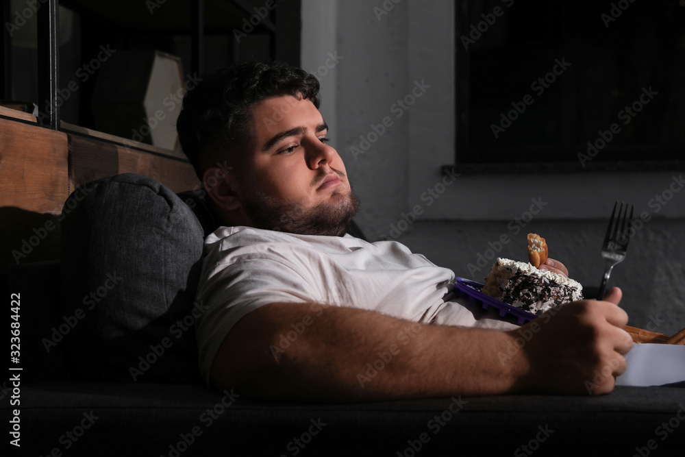 Depressed overweight man eating sweets in living room at night Stock ...