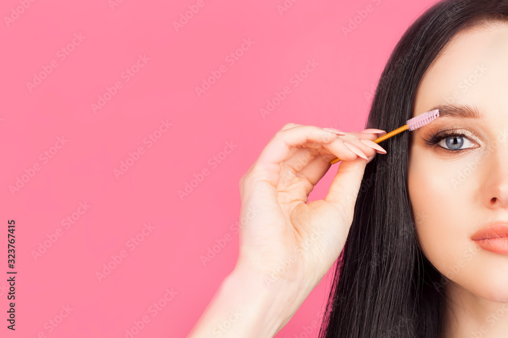 Half of the girl's face on a pink background, she holds an eyebrow comb ...