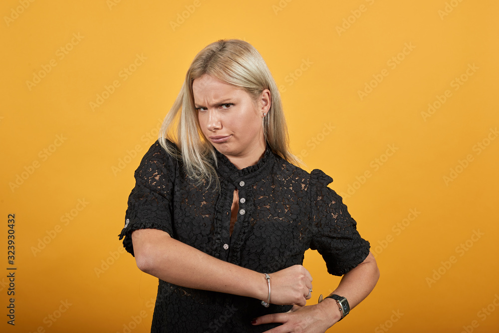 Beautiful blonde girl in black dress on yellow background an irritated ...
