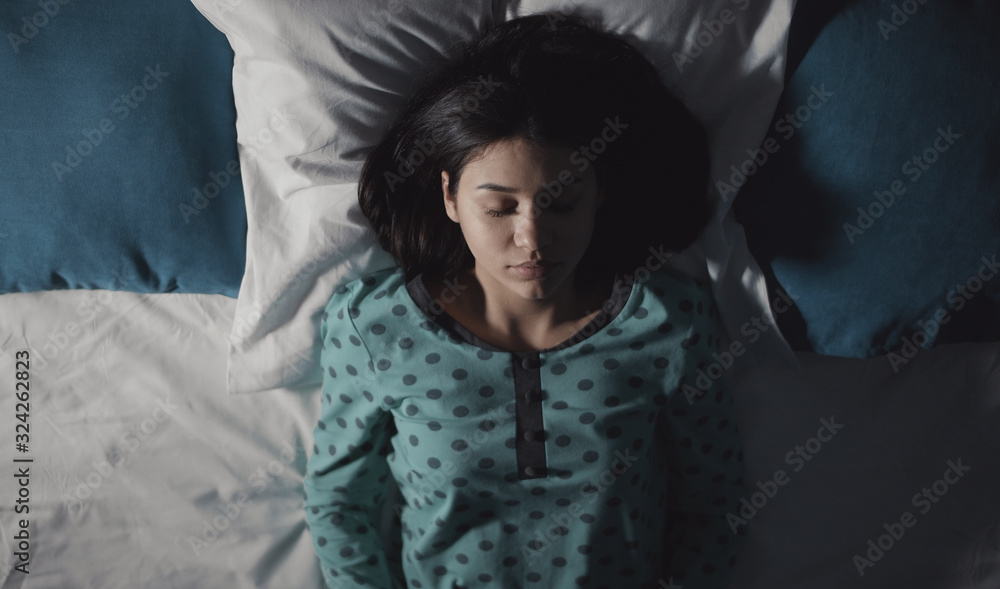 Portrait of dark-haired girl in pajamas lying on back sleeping in bed ...