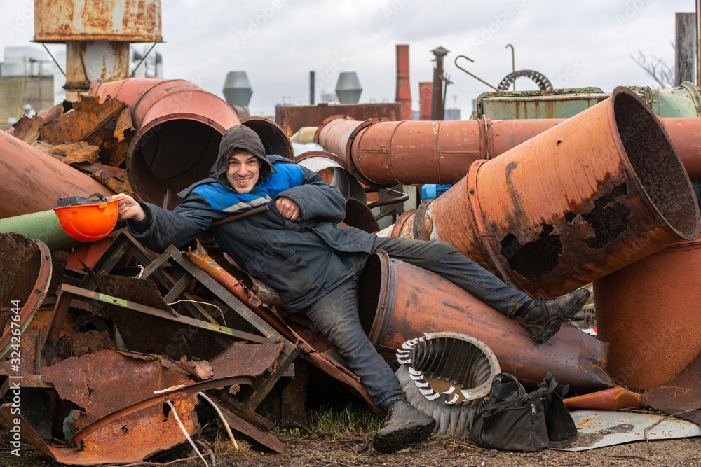 builder lies on a pile of scrap metal, taking off his helmet. man ...