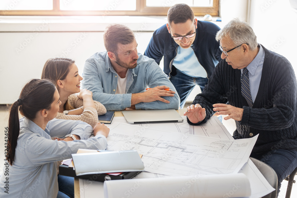 Architecture professor examining blueprint with group of his students ...