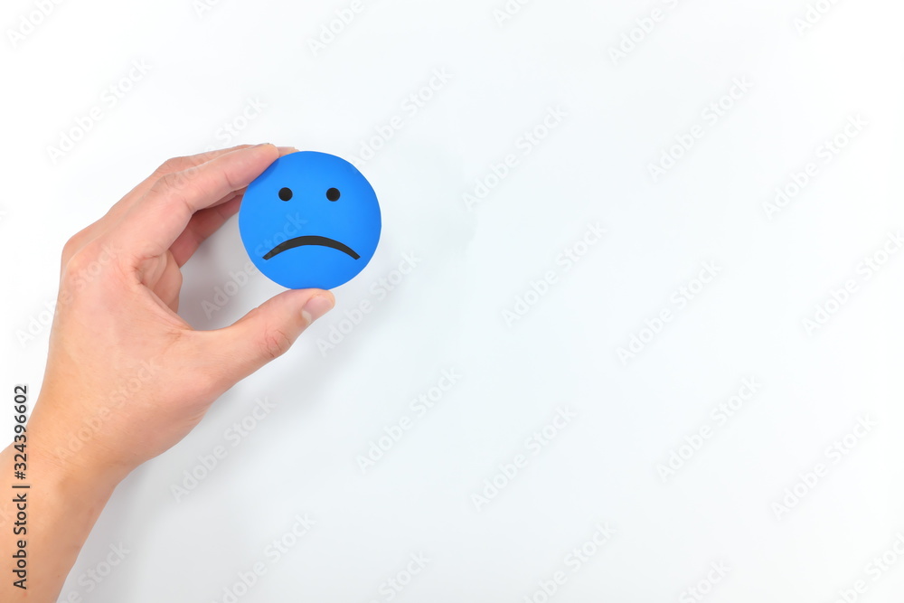 Hand holding a sad emoticon in white background. Sadness and ...